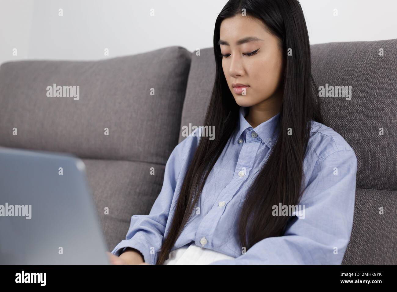 Asian BIPOC female works on laptop computer on couch. Focused ...