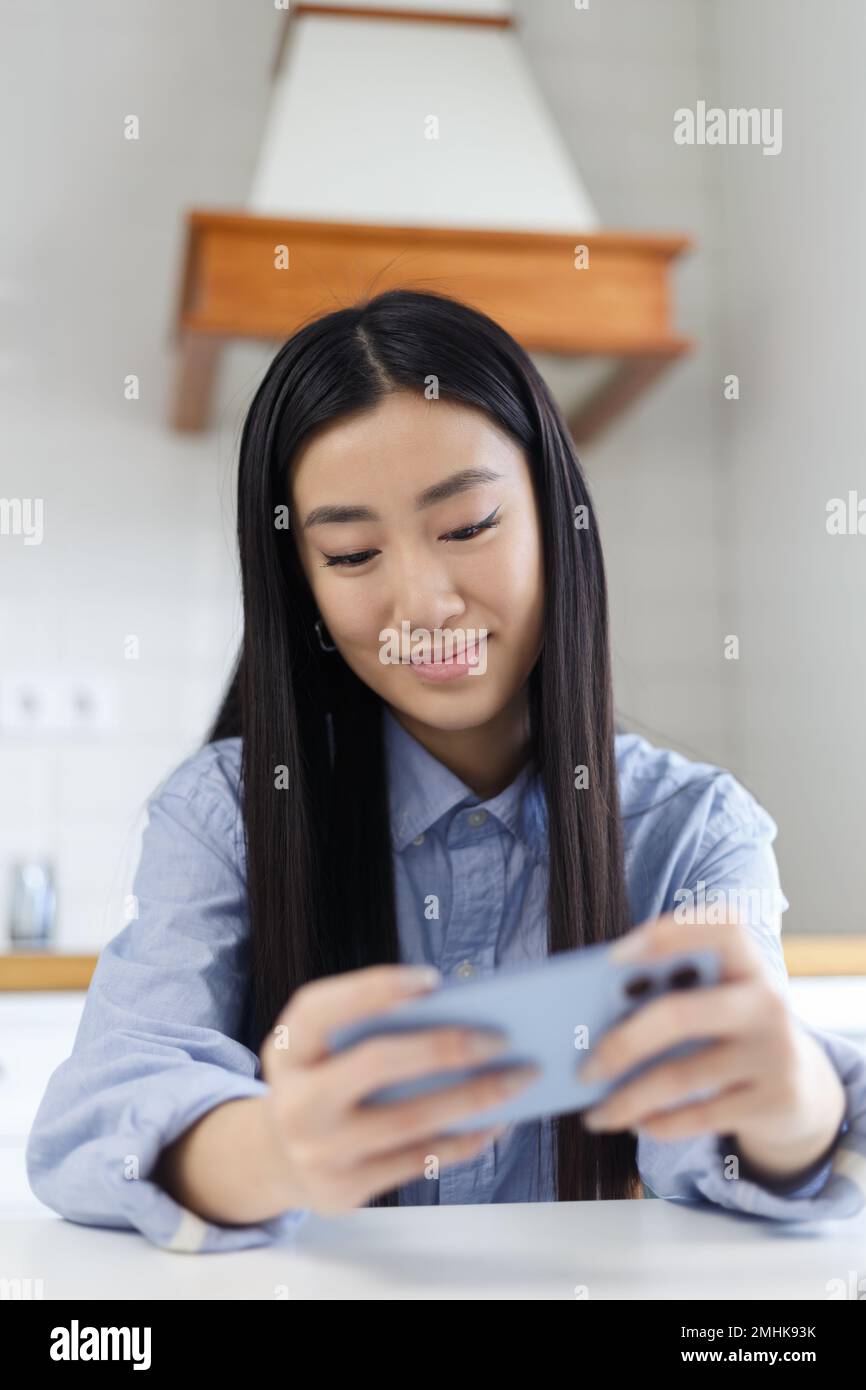 Gamer girl plays mobile game on smartphone. Cheerful Vietnamese BIPOC ...