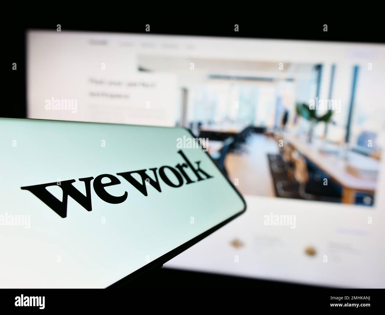 Smartphone with logo of American coworking space company WeWork Inc. on screen in front of ...