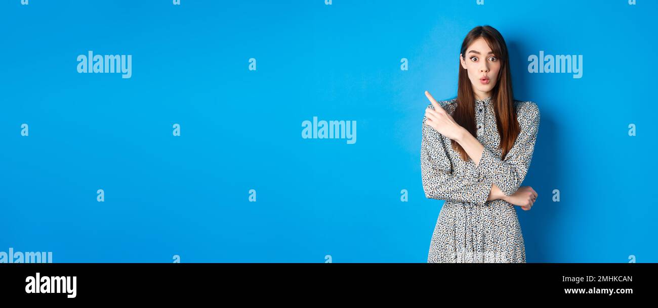 Excited young woman say wow, looking impressed and pointing left at ...