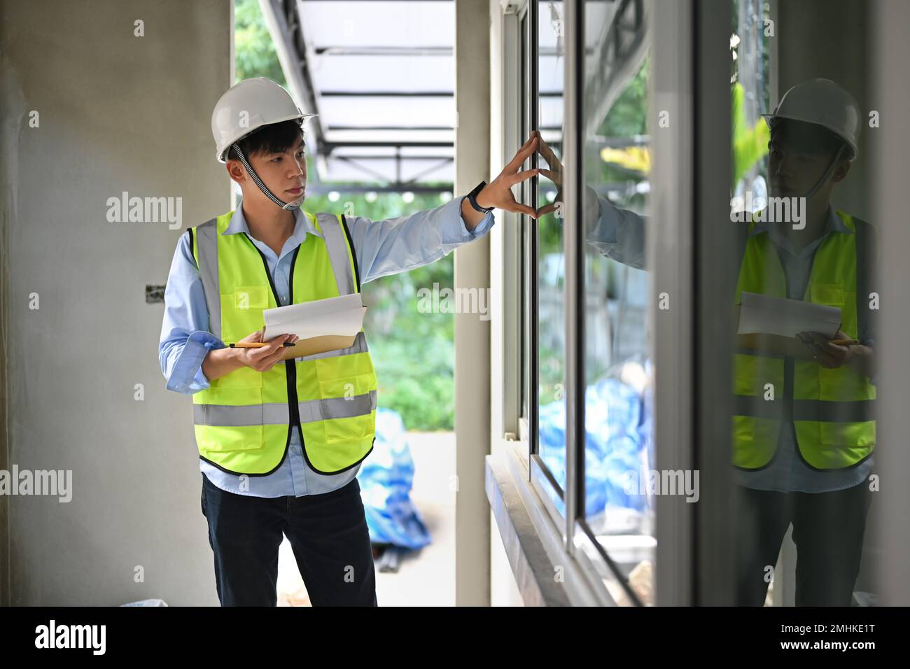 Asian man inspector in safety helmet and vest holding clipboard ...