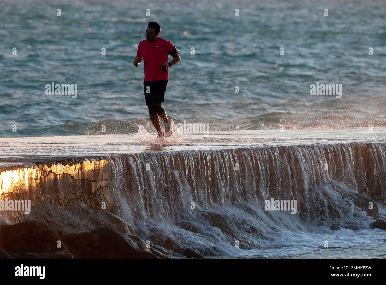A wave rolls over a jetty as a jogger sloshes through, Sunday, Nov. 10 ...