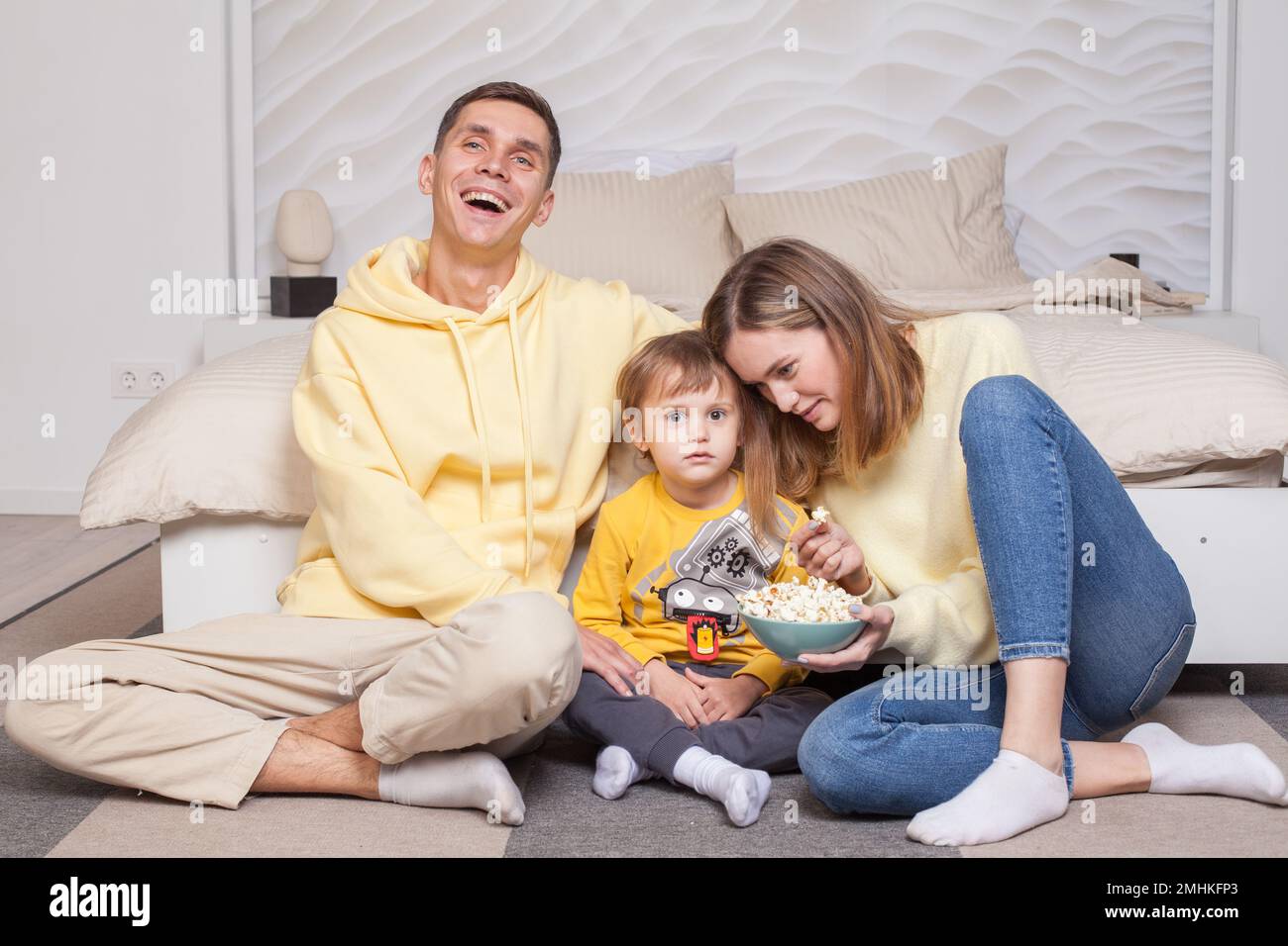 Laughing friendly family, parents with child son sitting by the bed and ...