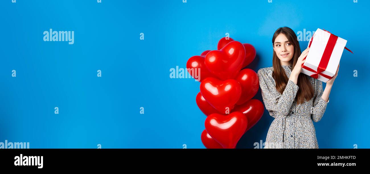 Valentines day. Beautiful woman shaking gift box to guess what inside ...