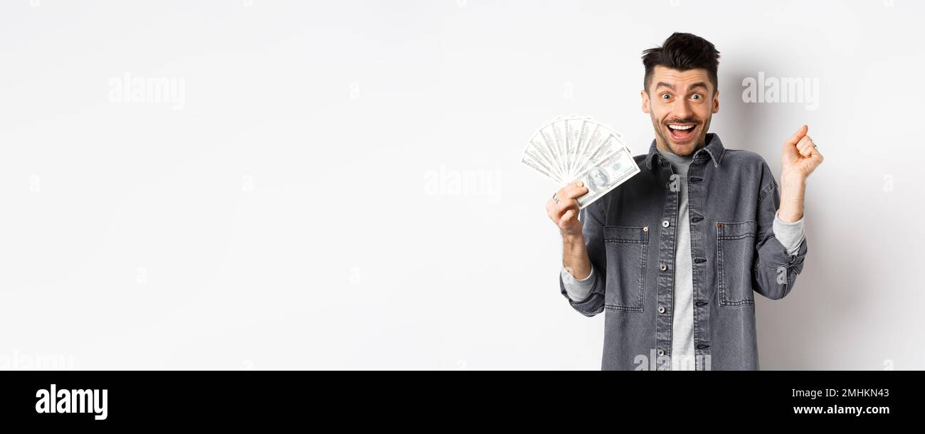 Cheerful young man jumping from excitement and showing dollar bills ...