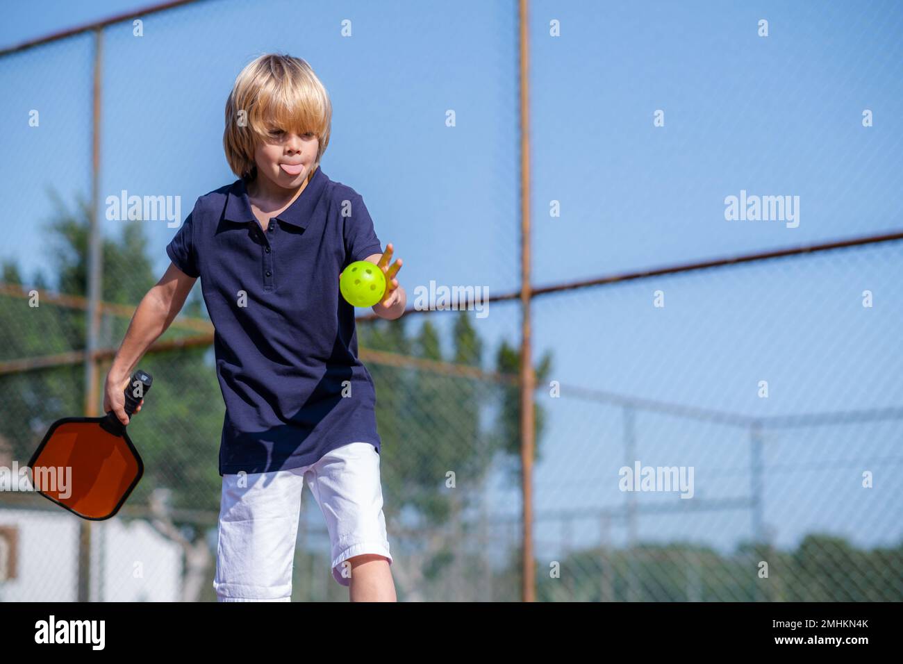 Happy blonde boy playing pickleball game, hitting pickleball yellow ...