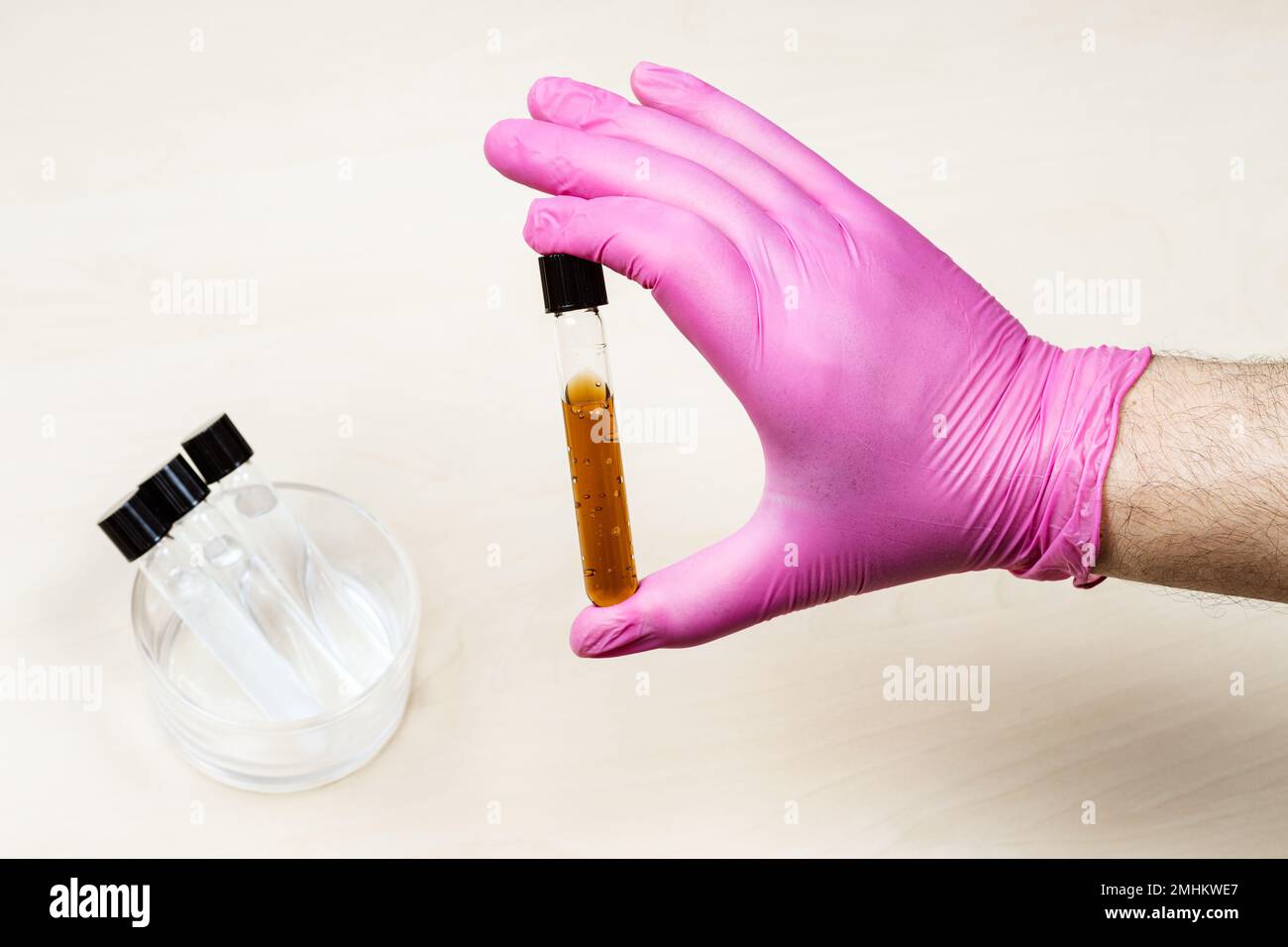 gloved hand holds test tube with brown liquid over light table with ...
