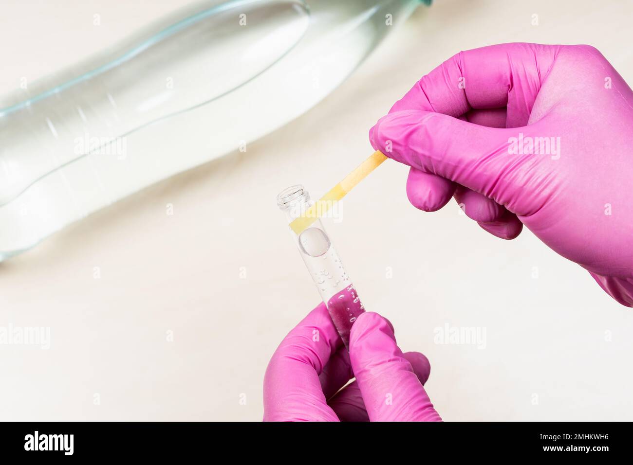 gloved hand holds neutral litmus paper on test tube with sample of ...
