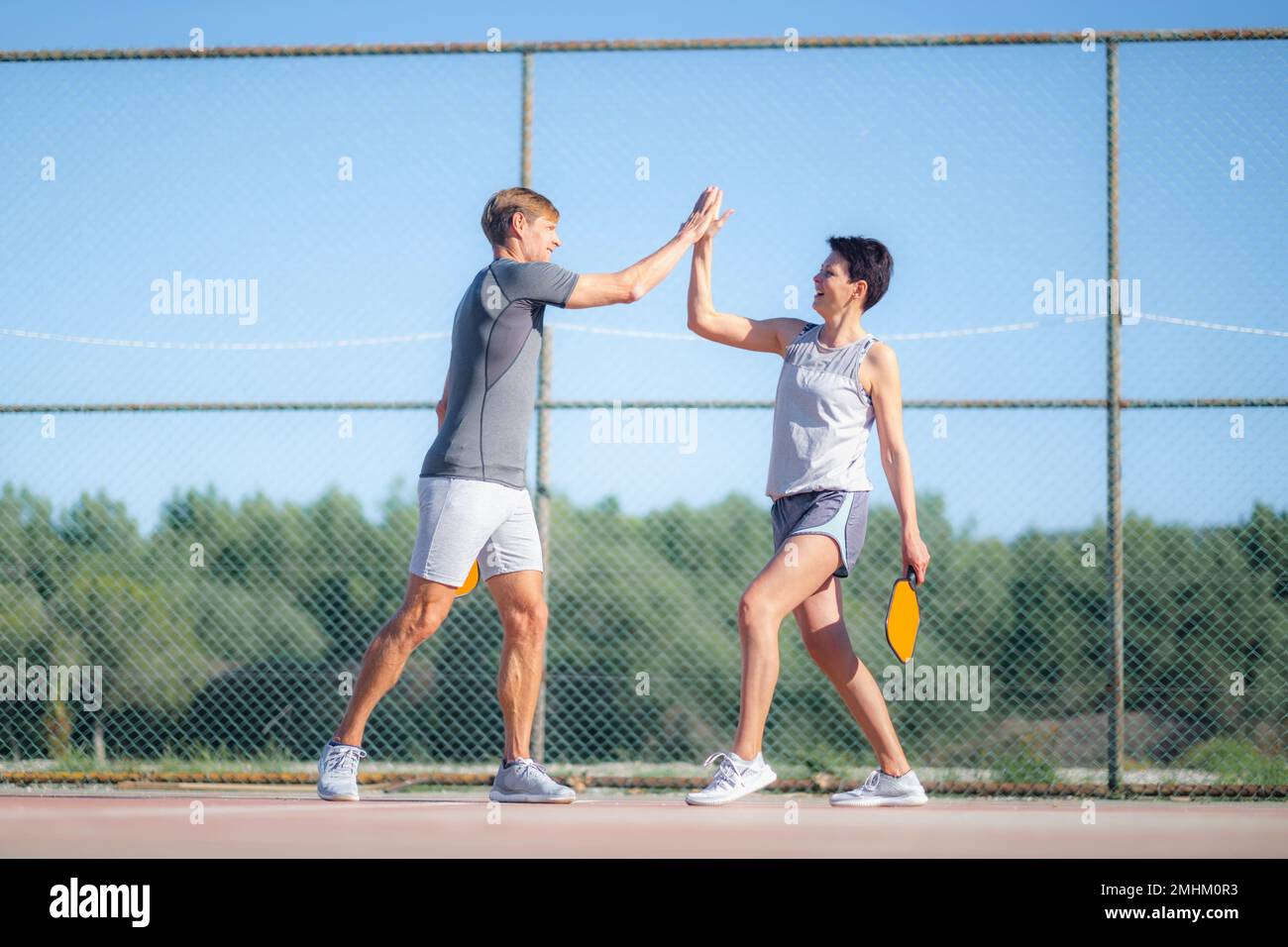Laughing couple playing pickleball game, hitting pickleball yellow ball ...