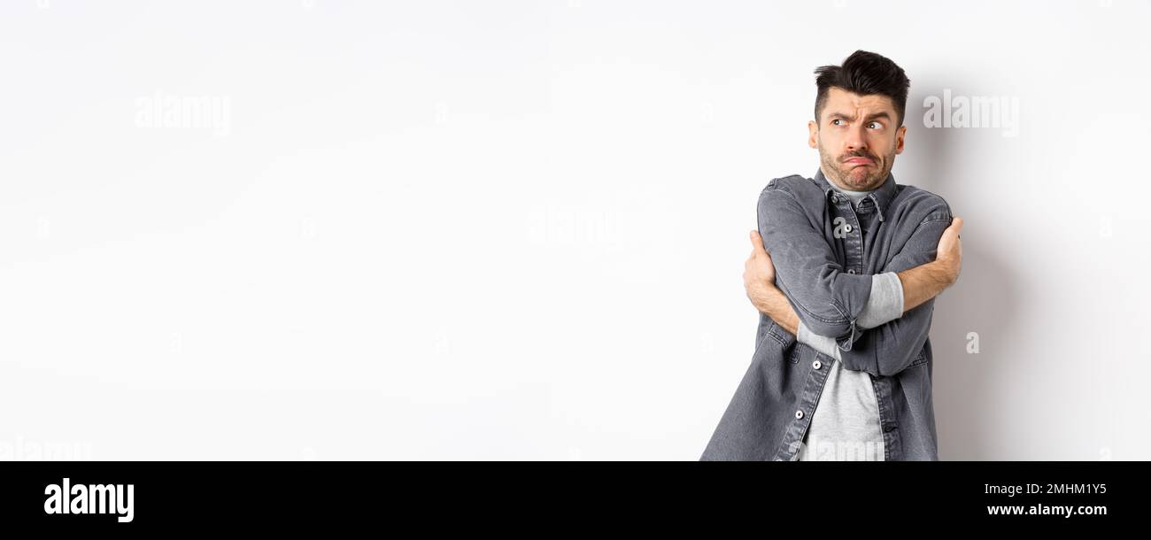 Displeased young man feeling discomfort, hugging himself and staring ...