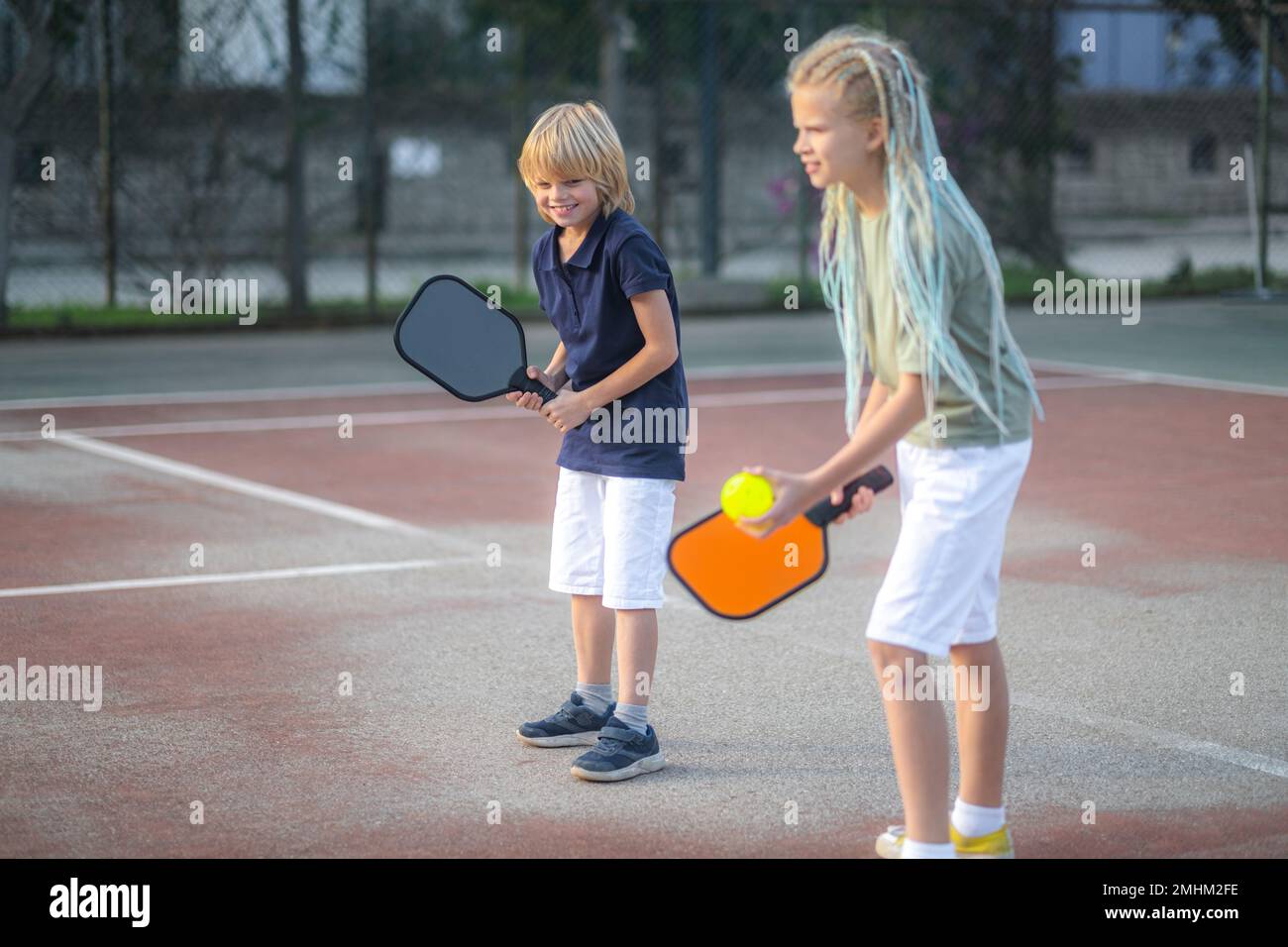 Laughing boy and girl playing pickleball game, hitting pickleball ...