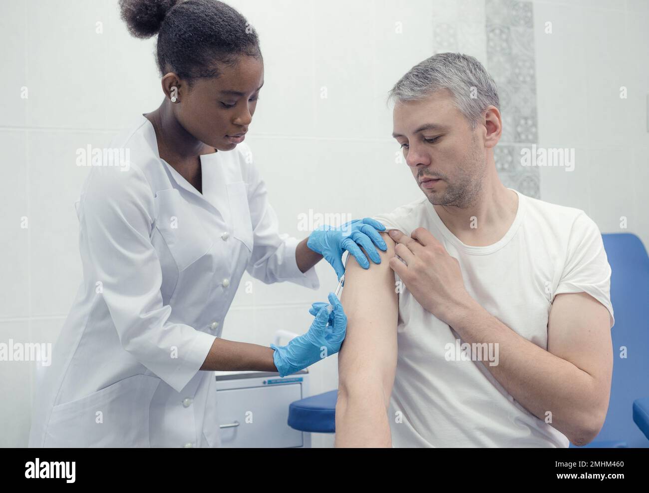 African-American female doctor gives an injection inoculation in the arm of a male patient Stock ...