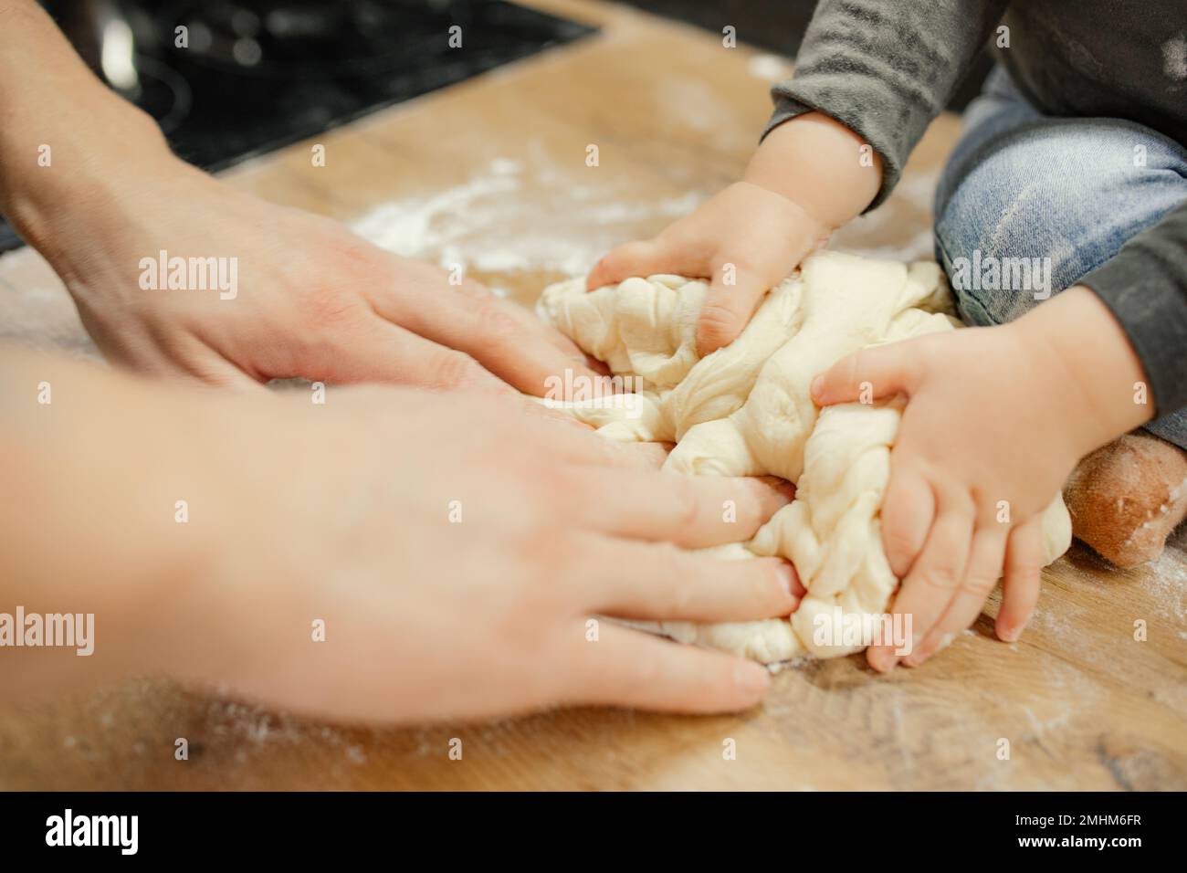 Parent with baby together knead raw elastic dough on kitchen tabletop ...