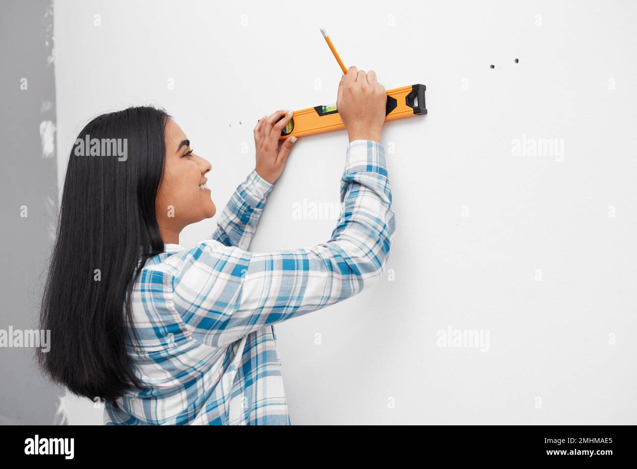 A young woman smiles while using spirit level against wall doing home ...