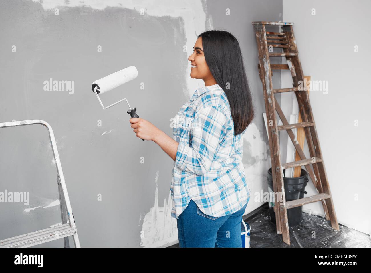 A young Indian woman prepares to paint a wall during home DIY project ...