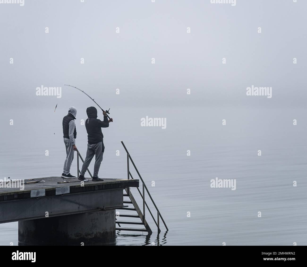 Unrecognisable people fishing in the fog on a pier or jetty. An ...