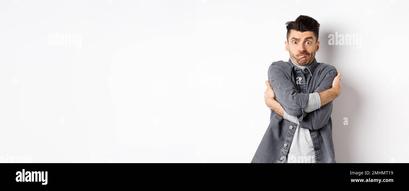 Funny young man hugging himself and grimacing, feeling embarrassed and ...