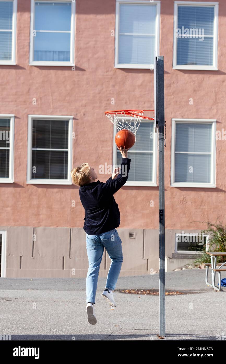 Teenage boy playing basketball in schoolyard Stock Photo - Alamy