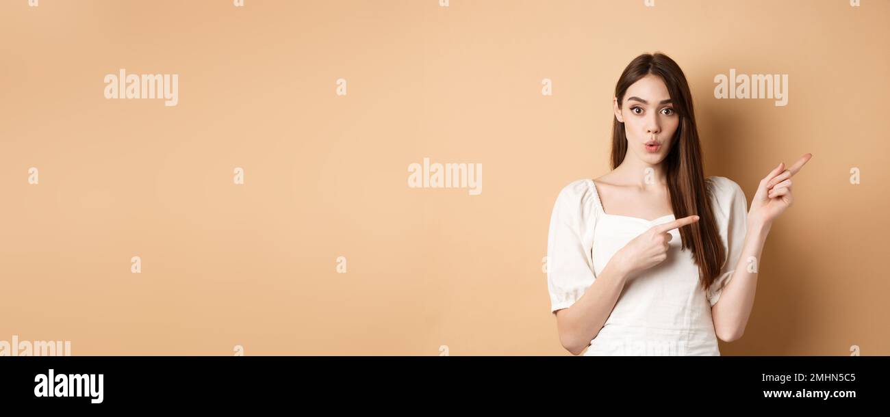 Wow look here. Impressed caucasian woman in white dress pointing ...