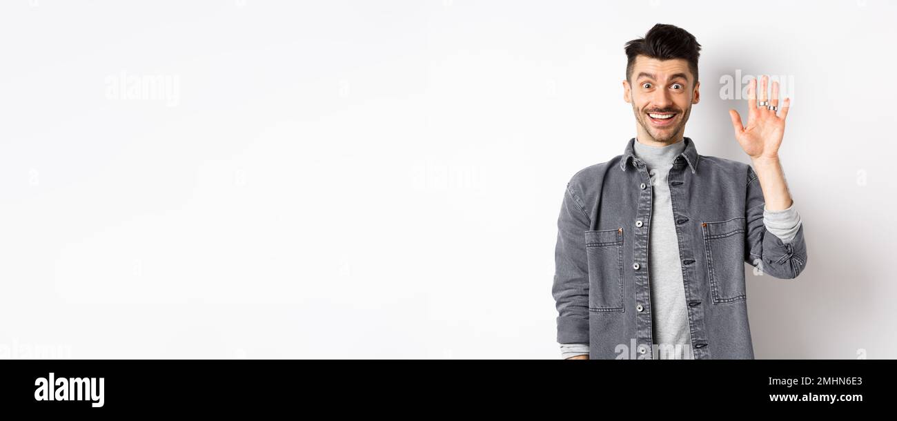 Friendly stylish man saying hello and waiving hand, smiling cheerful ...