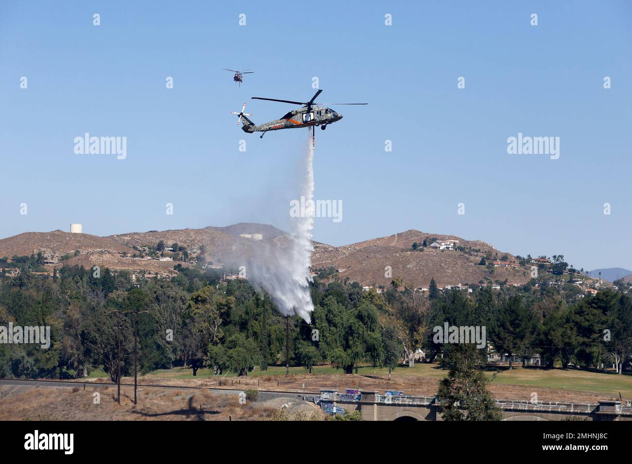A helicopter drops water to put out hotspots in a wildfire in Riverside ...