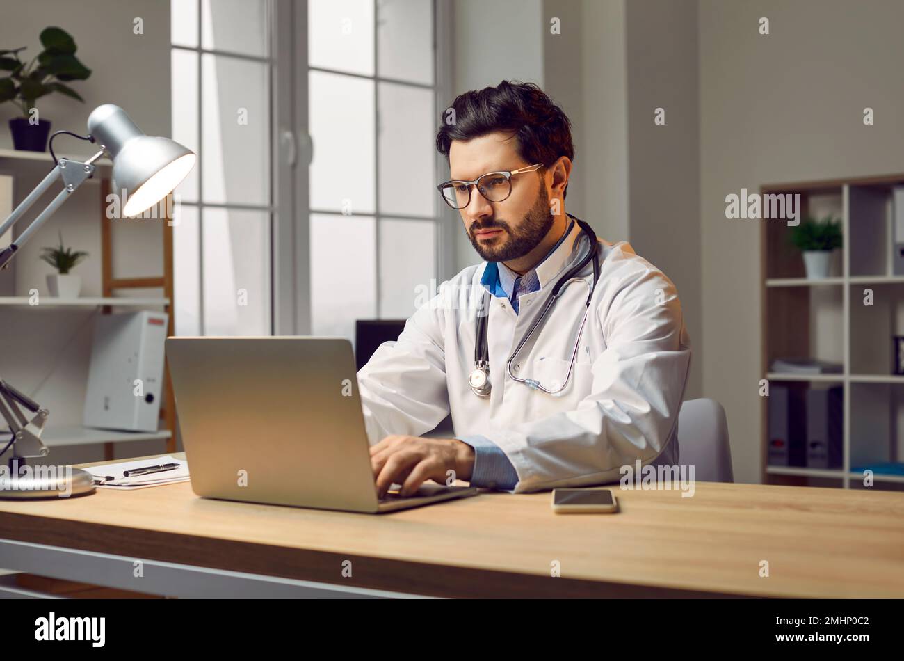 Professional male doctor filling documents using laptop computer Stock ...