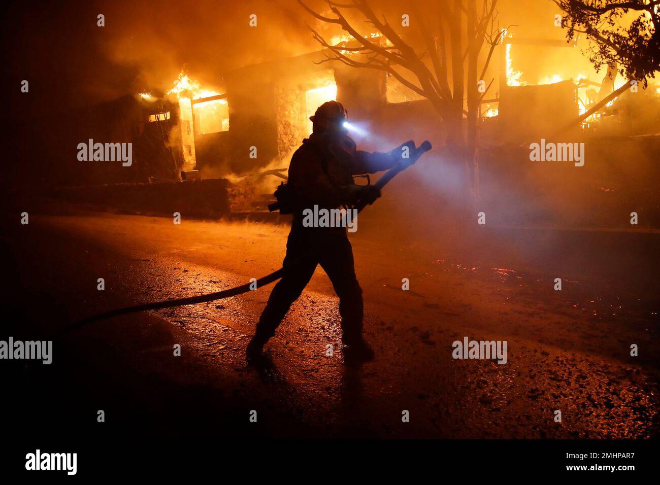 A firefighter gets in position to hose down flames as a home burns in ...
