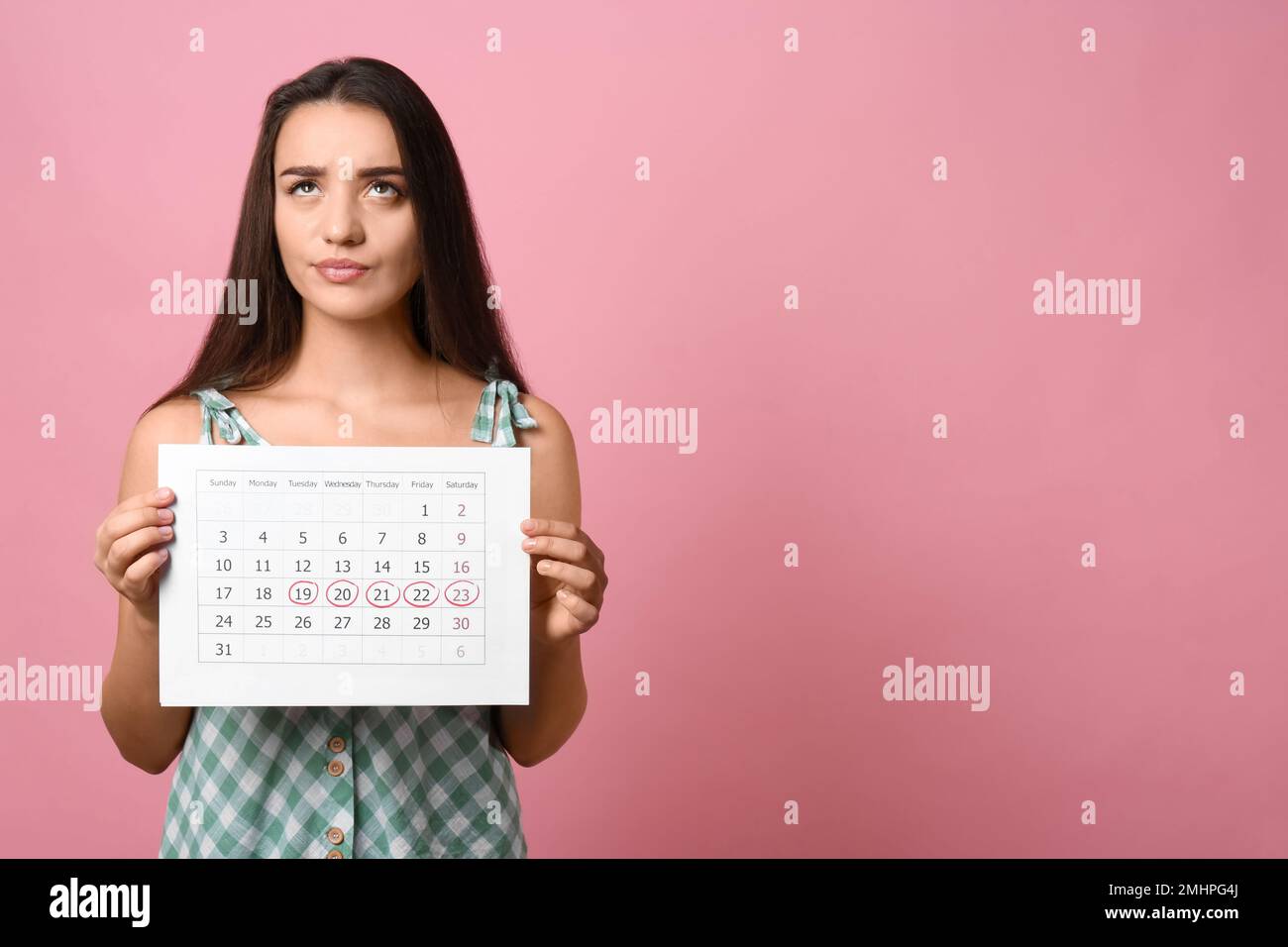 Young woman holding calendar with marked menstrual cycle days on pink ...