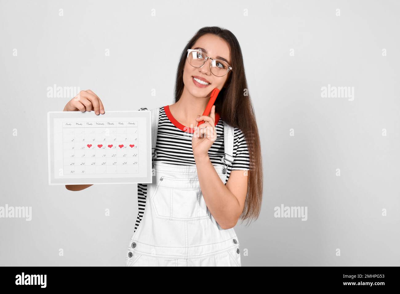 Young woman holding calendar with marked menstrual cycle days on light ...