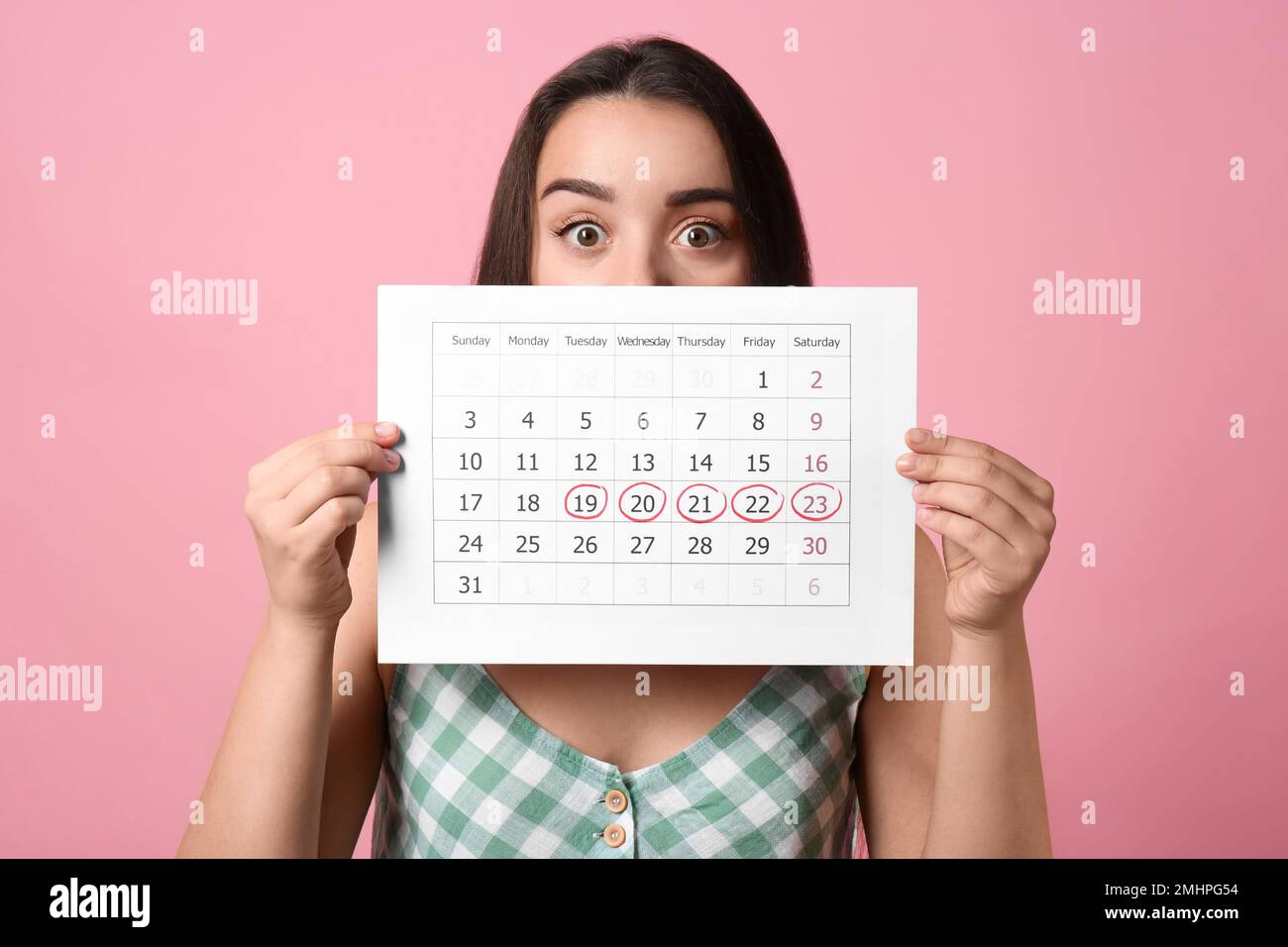 Young woman holding calendar with marked menstrual cycle days on pink ...