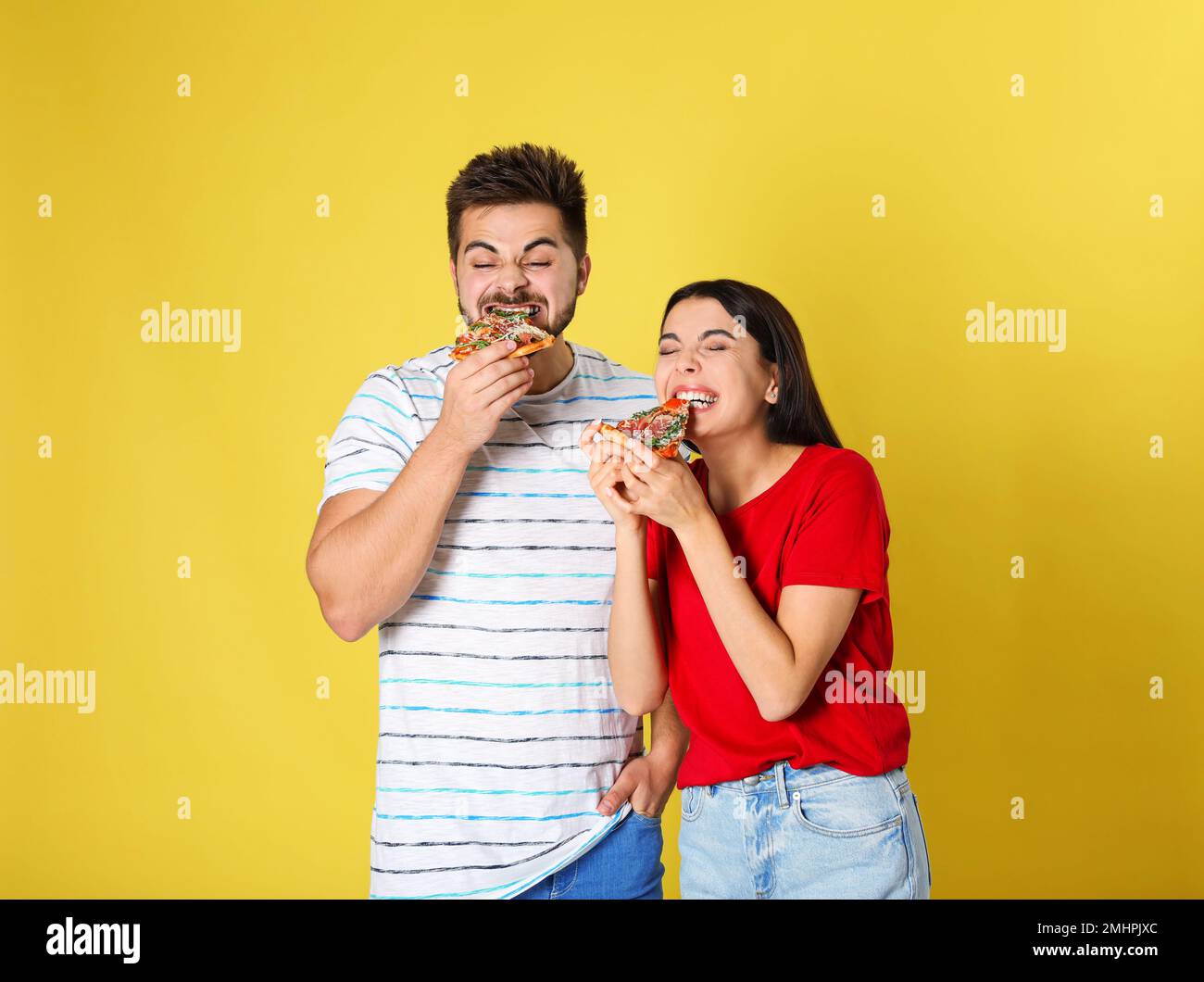 Emotional couple eating pizza on yellow background Stock Photo - Alamy