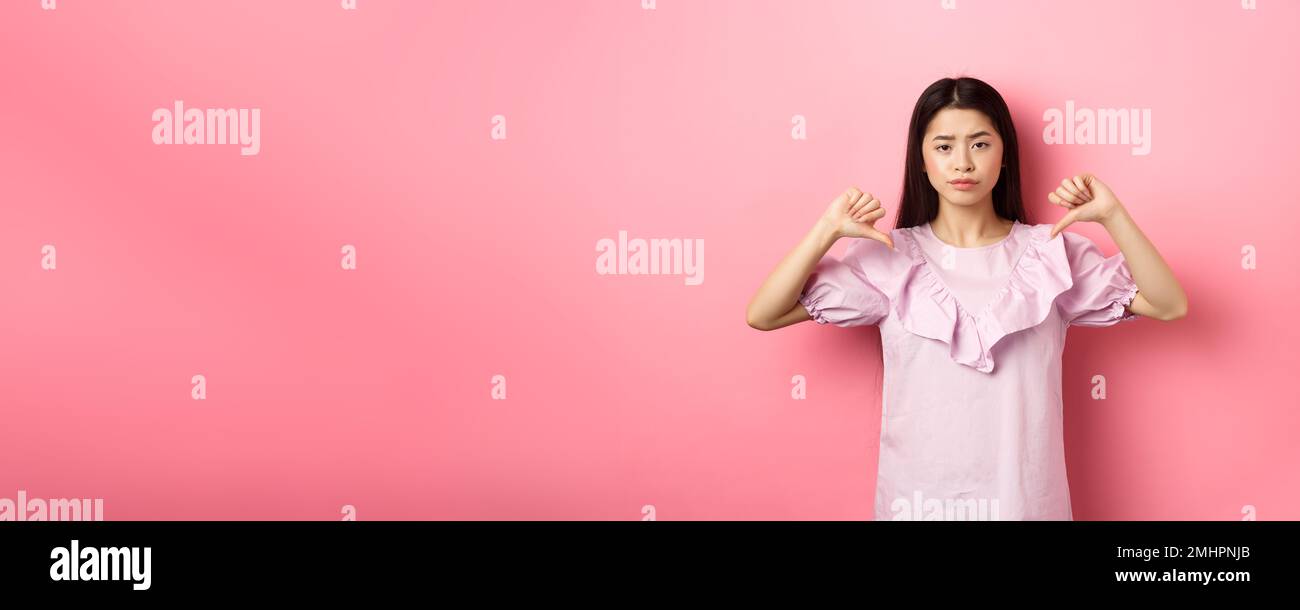 Skeptical and disappointed asian woman showing thumbs down with ...