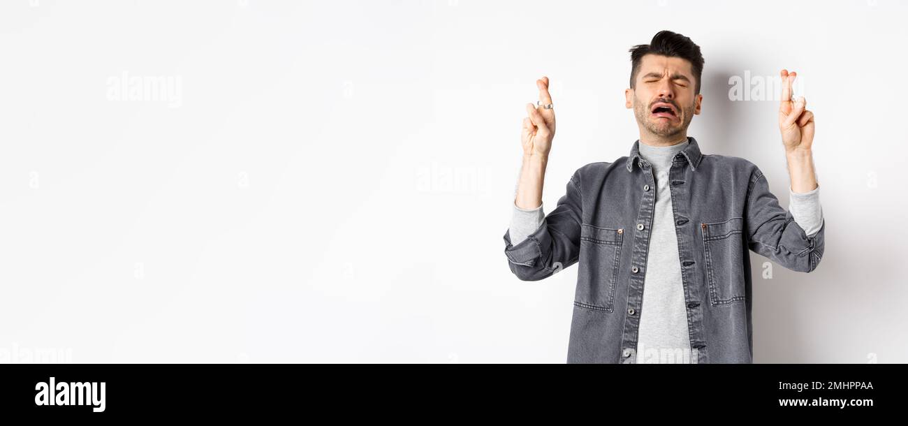 Sad and miserable man hoping god, cross fingers and crying, praying or ...