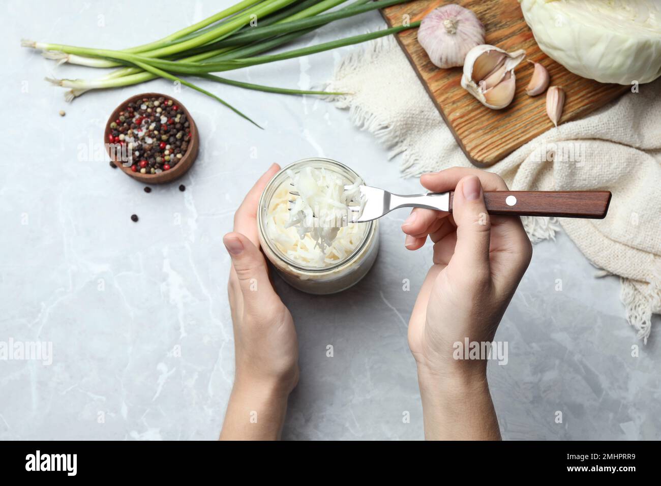 Woman eating fermented cabbage at light grey marble table, top view ...