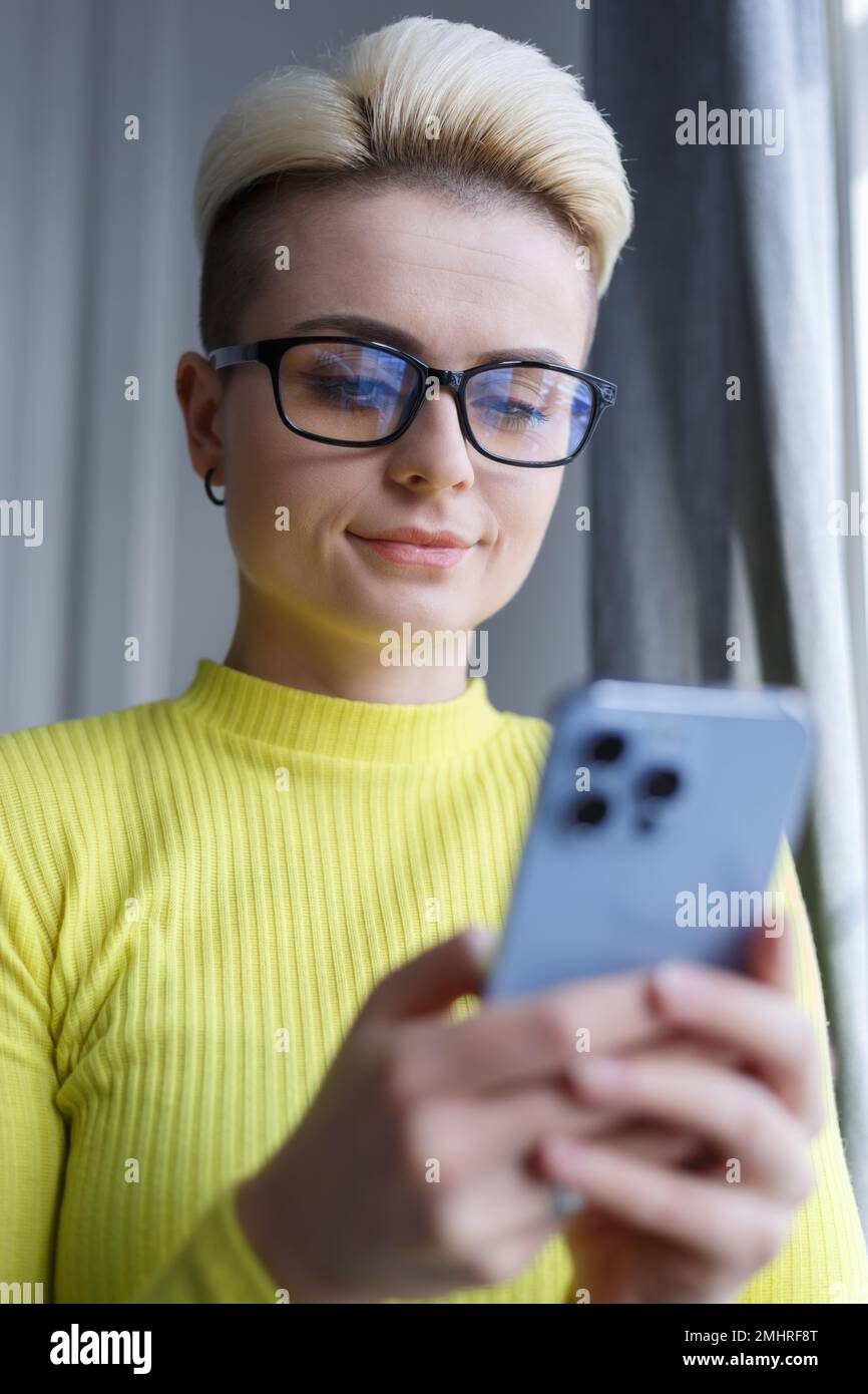 Tom boy female with short blond hair typing sms message on smartphone ...