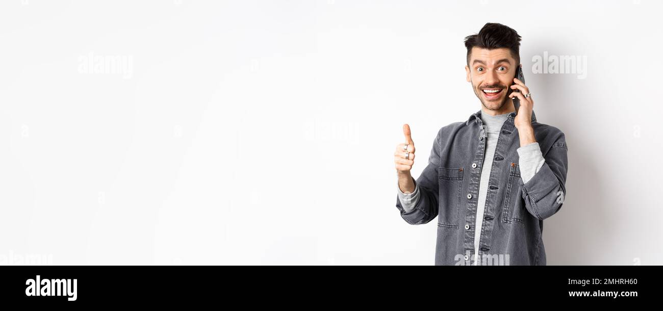 Excited young man talking on phone and showing thumbs up, smiling ...