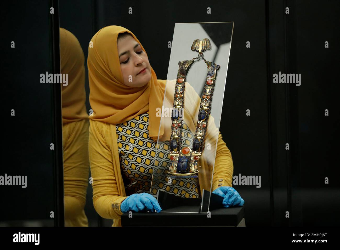 Restorer Olfat Mohamed poses for photographs with a gold inlaid pectoral, chain, and ...