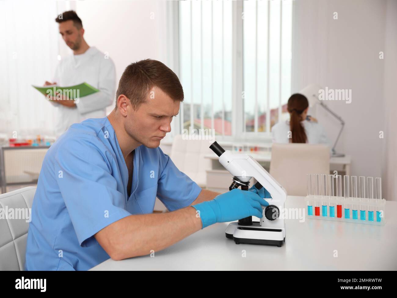 Scientist with microscope at table and colleagues in laboratory ...
