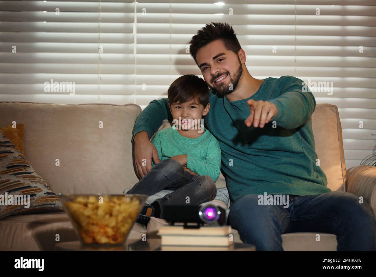 Young man and his son watching movie using video projector at home ...