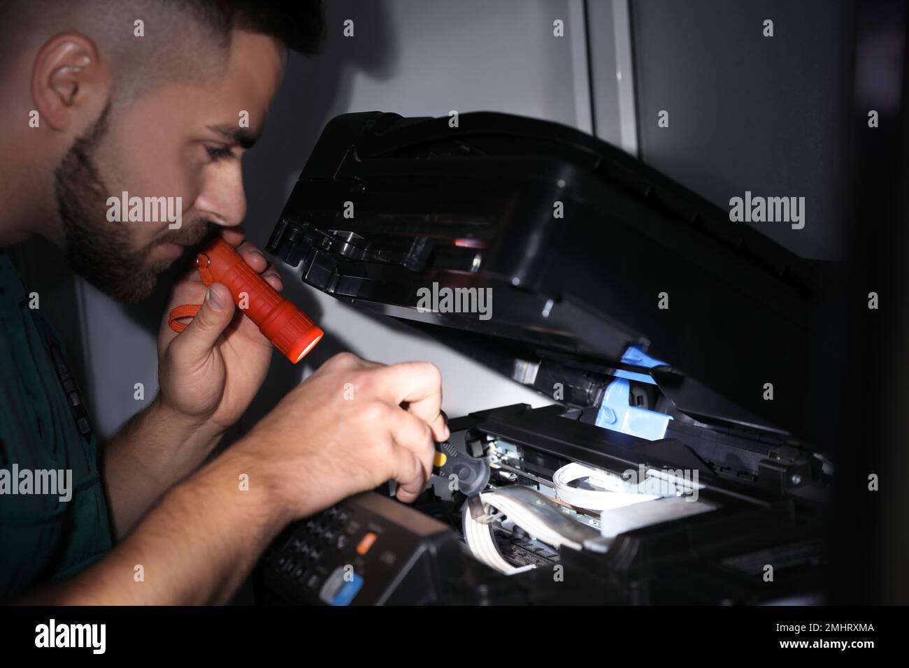 Repairman with flashlight fixing modern printer indoors Stock Photo - Alamy