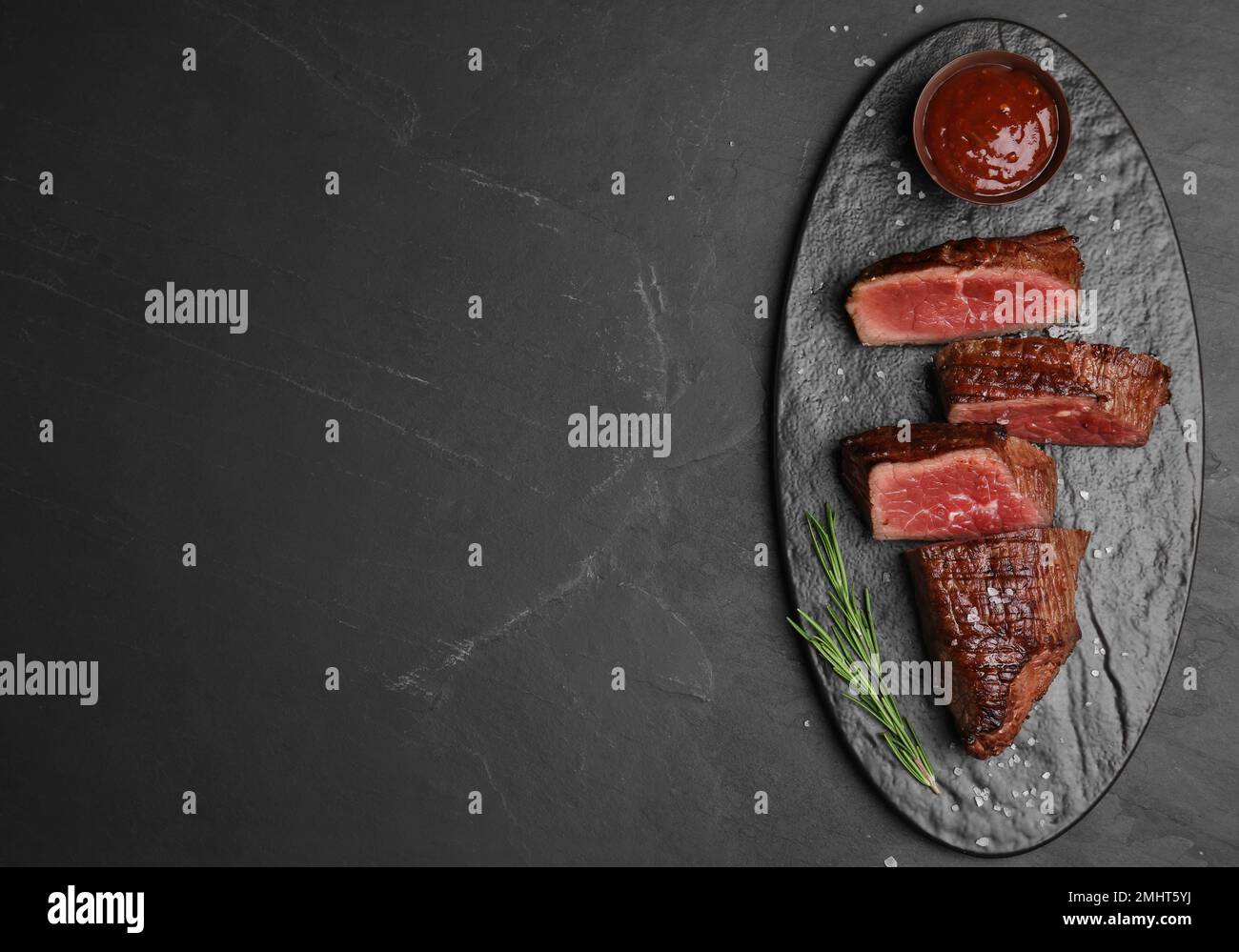 Delicious sliced beef tenderloin on black table, top view. Space for ...
