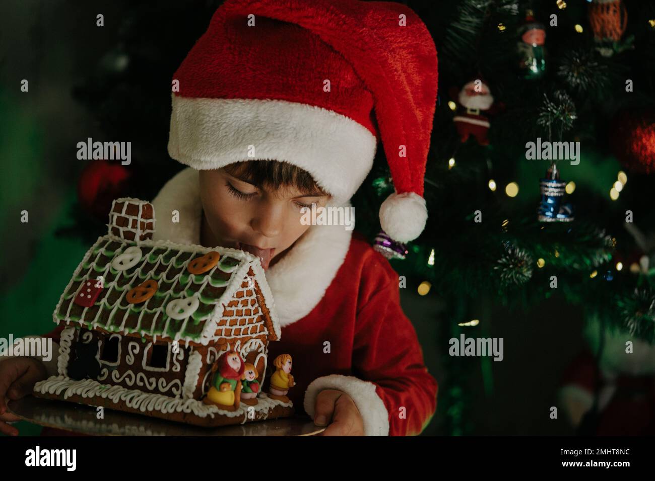 Cute little boy in Santa Claus costume eating gingerbread house ...
