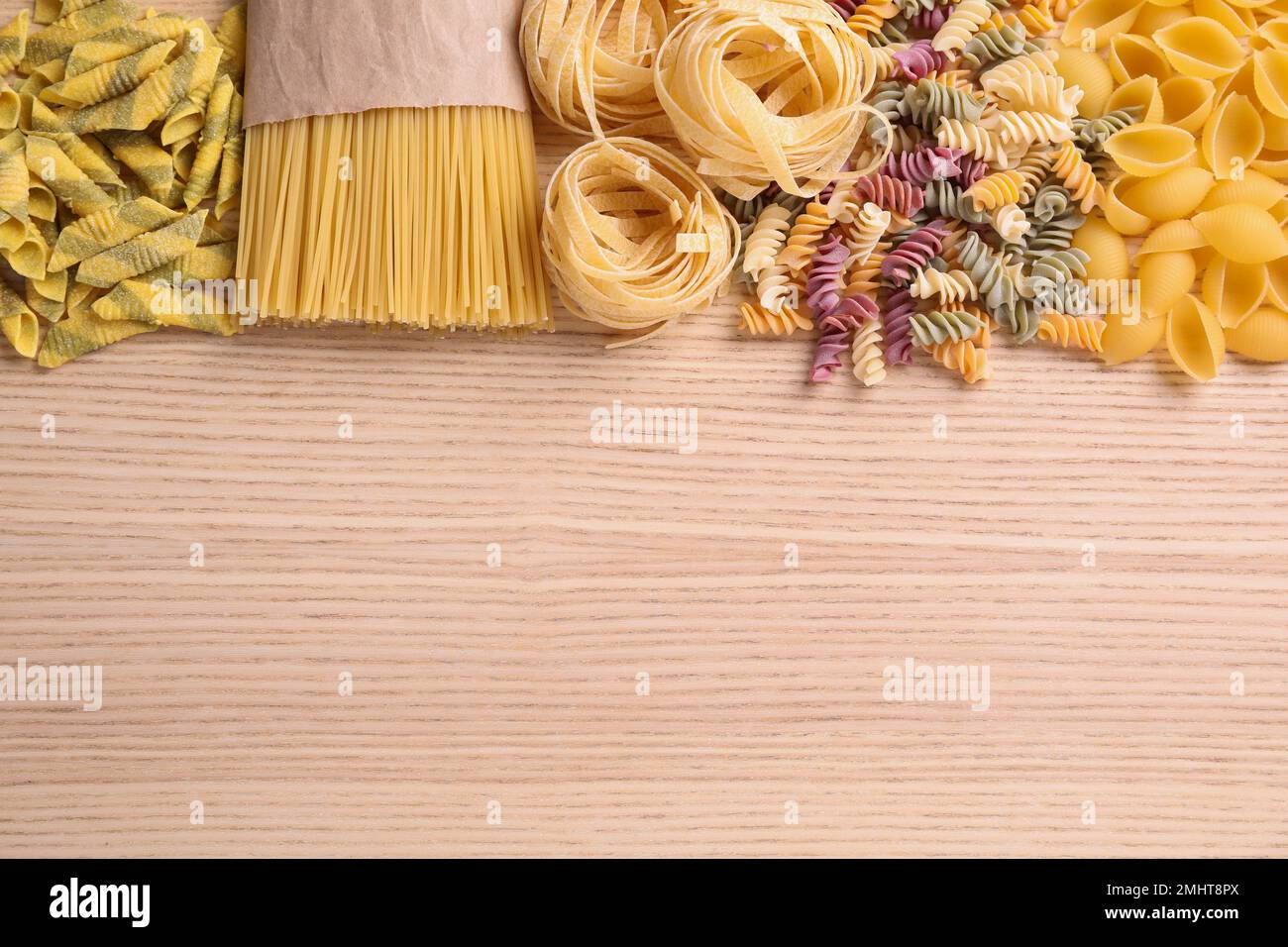 Different types of pasta on wooden table, flat lay. Space for text ...