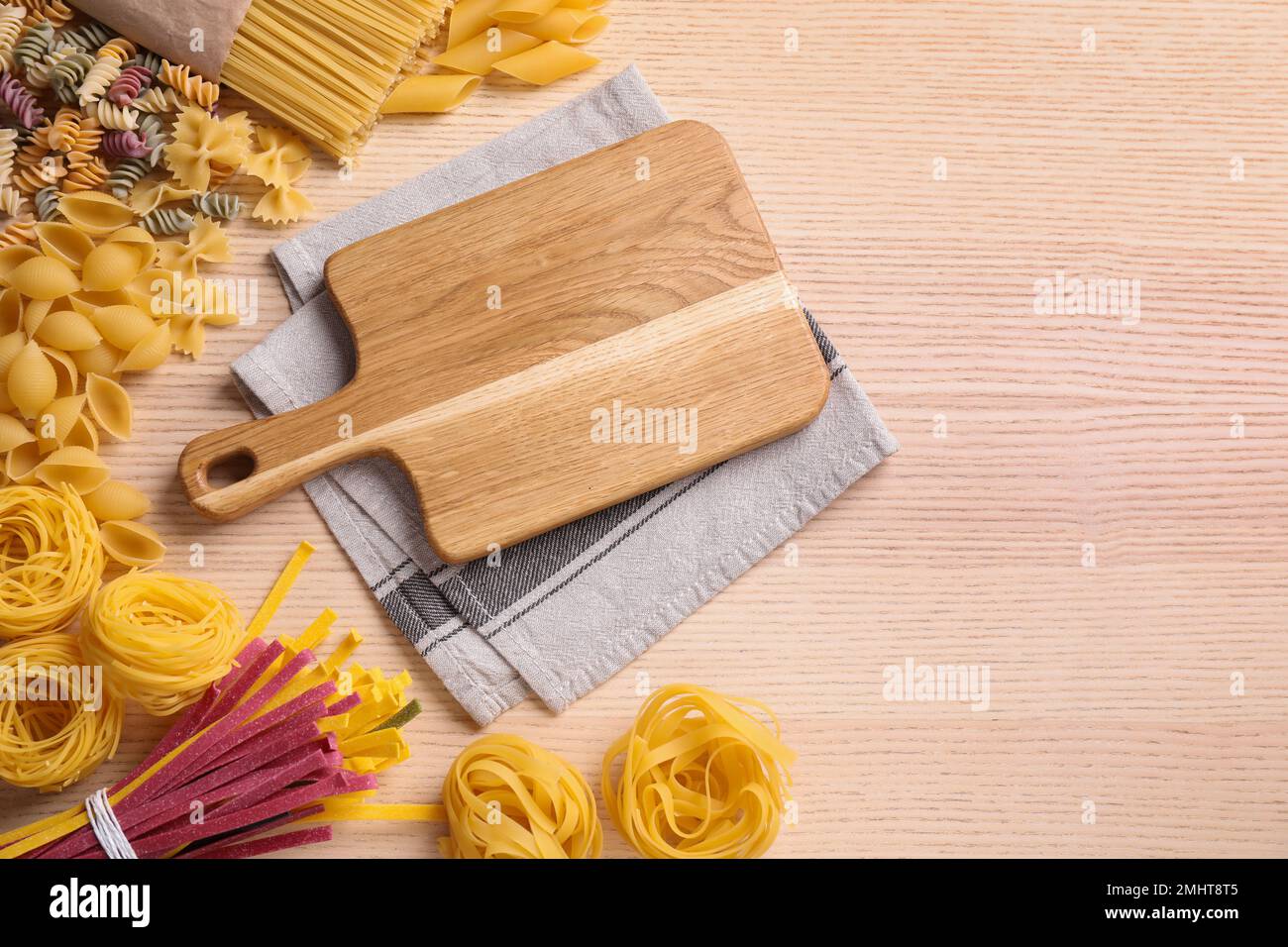 Different types of pasta and cutting board on wooden table, flat lay ...
