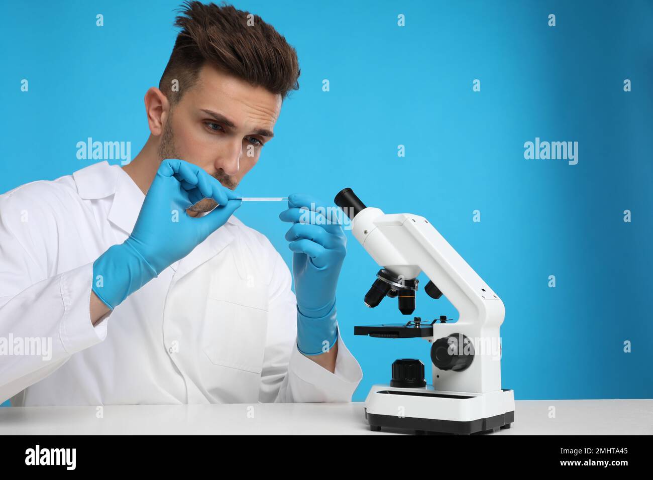 Man with slide and microscope at white table on blue background ...