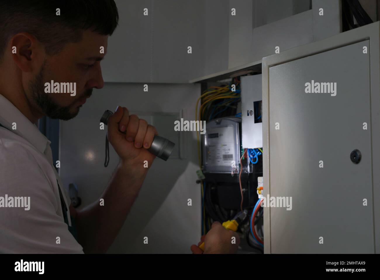 Electrician with flashlight fixing electric panel indoors Stock Photo ...