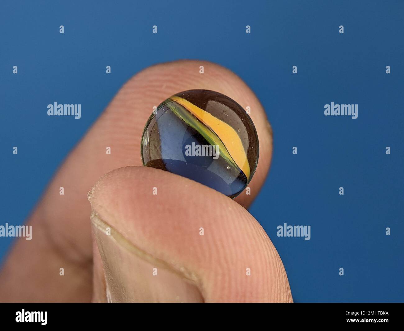 Closeup finger holding marble on a blue background Stock Photo - Alamy