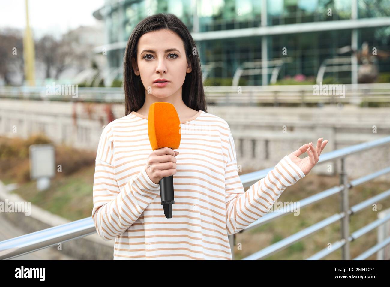 Young female journalist with microphone working on city street Stock ...