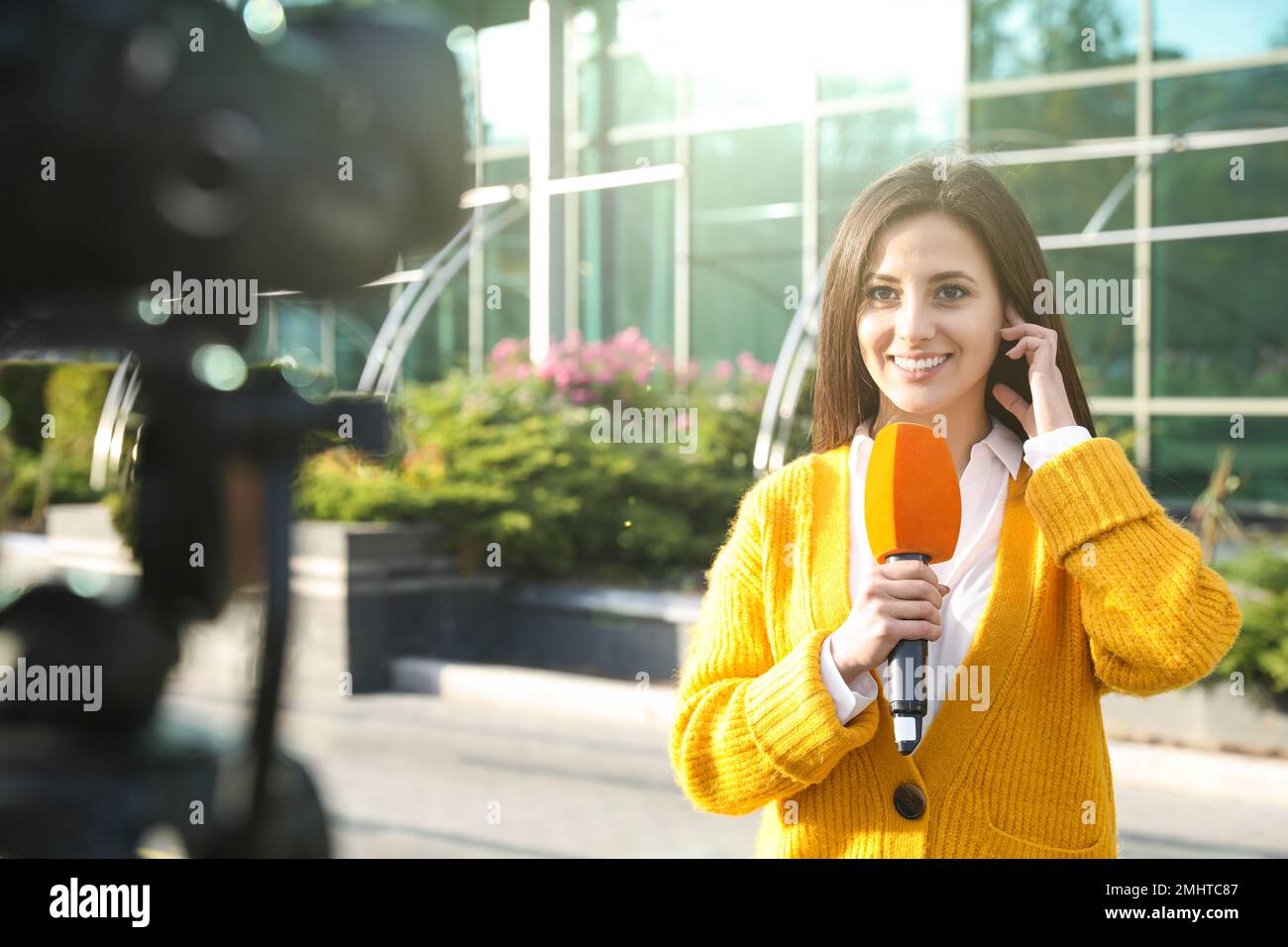 Young female journalist with microphone working on city street Stock ...