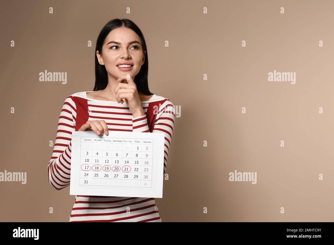 Pensive young woman holding calendar with marked menstrual cycle days ...